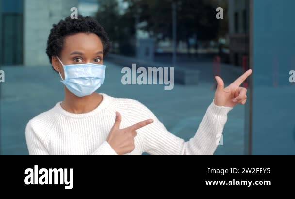 African woman in mask stands shows with hands direction to side. Mixed ...
