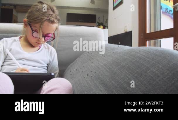 kid using tablet at home sitting on the couch. Little girl sitting on ...