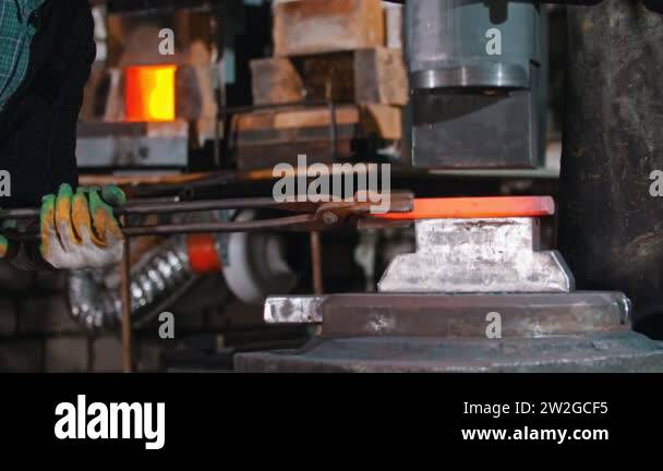 Blacksmith putting a longer piece of metal under the pressure of ...
