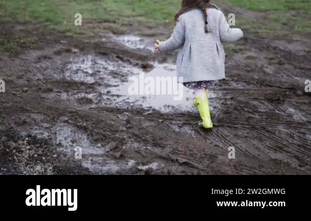 Happy little girl in yellow rain boots joyfully jumping in a muddy puddle Stock Video Footage ...