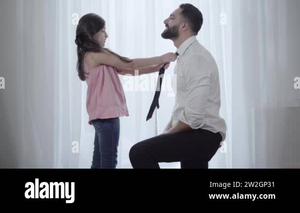 Side view of Middle Eastern little girl tying necktie of happy father ...