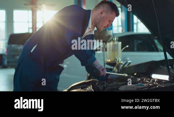Male Caucasian young auto mechanic standing at open car and repairing ...