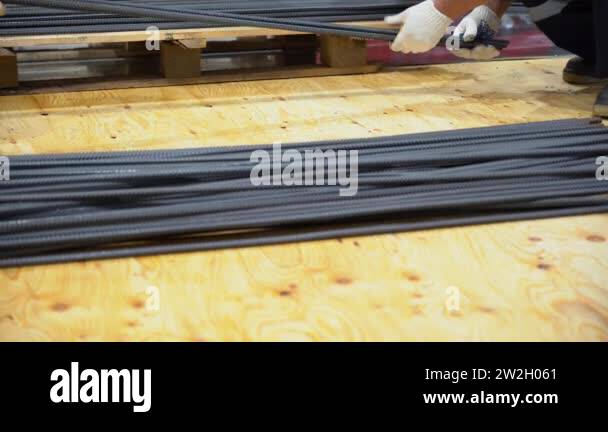 On the wooden floor are long bars of rebar. Workers people wear blue ...