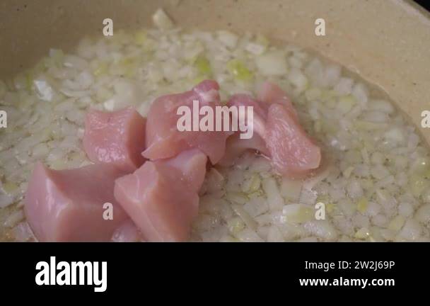 Chicken meat in cubes are being added in to the pan with frying onion ...
