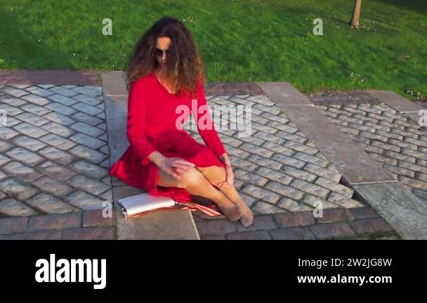 Drunk elegant lady in red dress sitting on stairs and staggers after ...