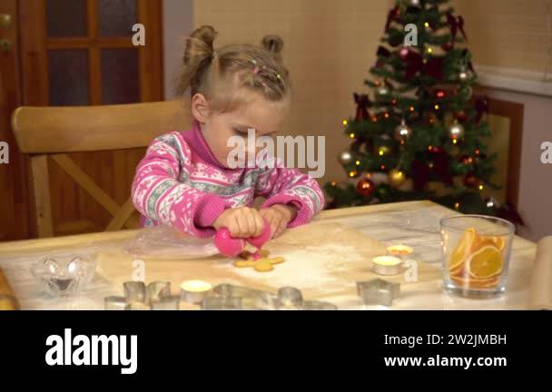 A girl decorates a gingerbread human shaped cookie with pink icing. The ...
