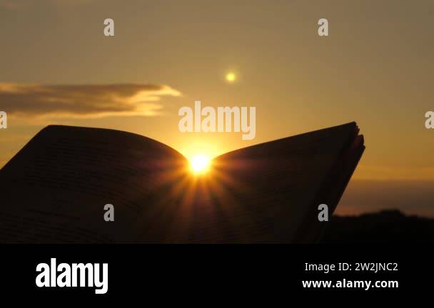 A person reads a book in the sun. Man reads Bible outdoors. A man holds ...