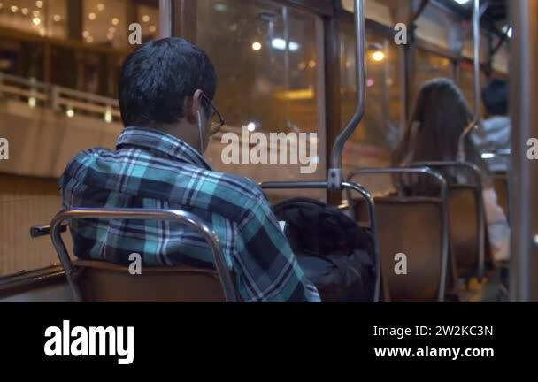 Chinese man from behind on a bus sitting alone and reading at night in ...