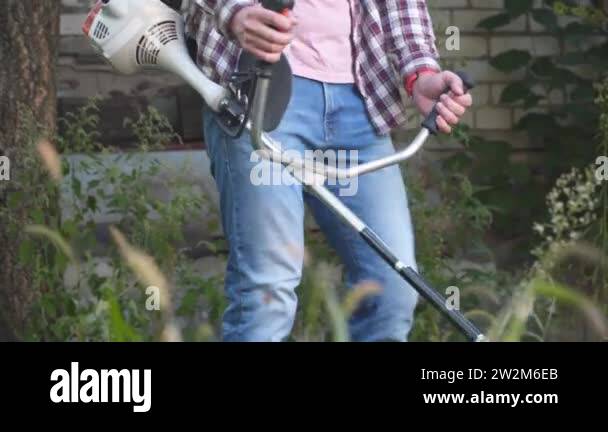 Young Caucasian farmer uses gasoline powered electric scythe to trim ...