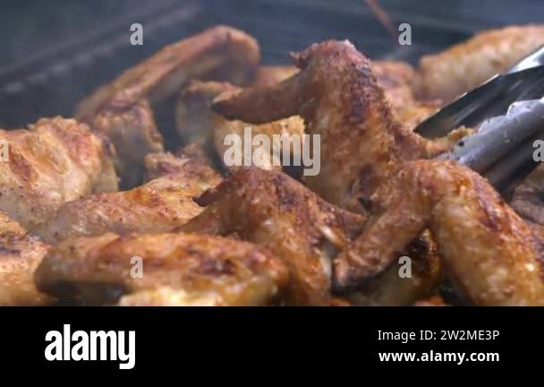 Man using metal tongs to turning some spicy chicken wings which are ...