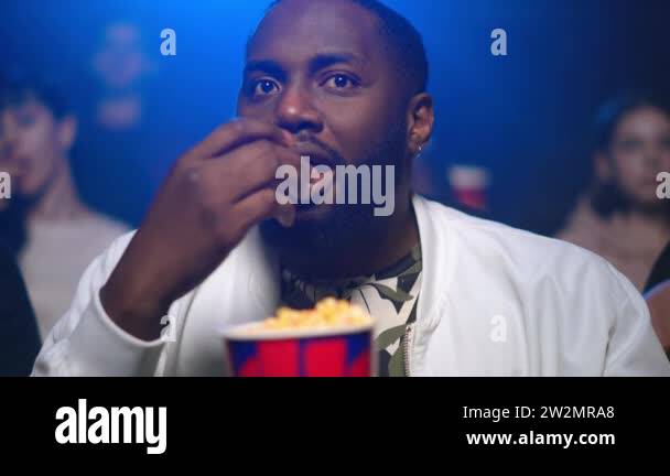 African man eating popcorn in movie theater. Afro american guy watching film Stock Video Footage ...