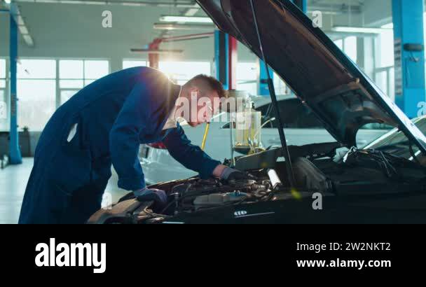 Male Caucasian young auto mechanic standing at open car and repairing ...