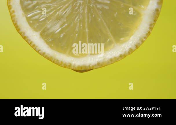 Close up or macro of a slice of lemon, a drop of water falls in slow motion. Concept of fresh ...