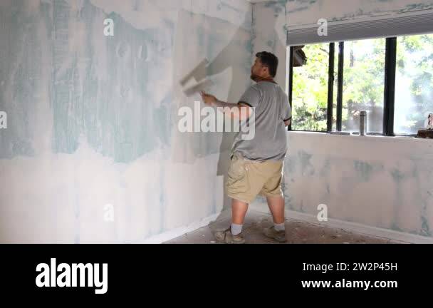 Construction worker plaster with trowel to gypsum board puts a ...