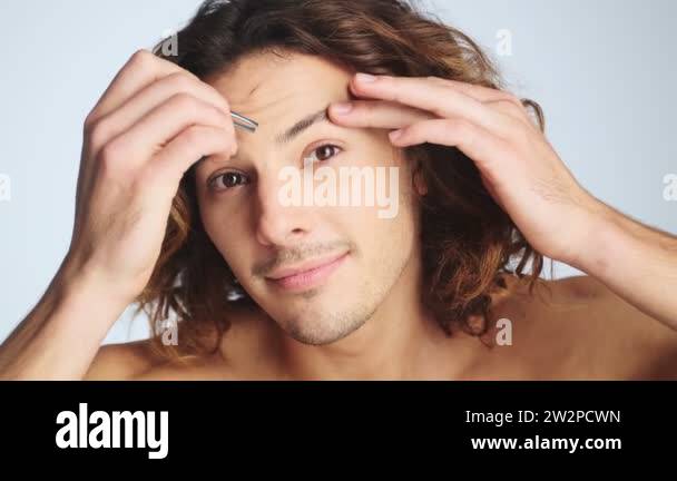 A focused man is correcting his eye brows using eyebrow tweezers while ...
