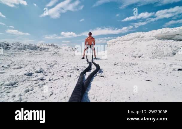 Bodybuilder trains his muscles with cable on the hill under blue sky ...