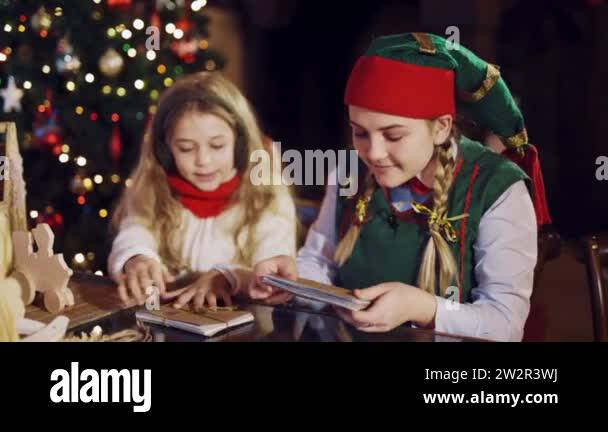 A funny elf is sitting at the table with a little girl and showing how ...