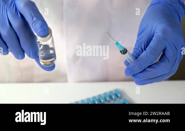 Doctor or nurse in blue gloves holding a syringe and transpaent bottle ...