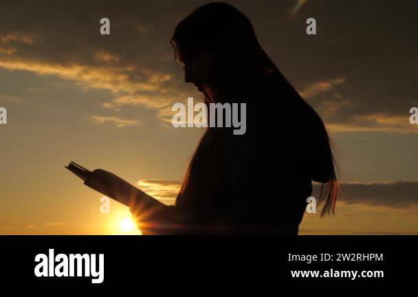 A woman reads a book in rays of the sun. Man reads Bible outdoors. A ...