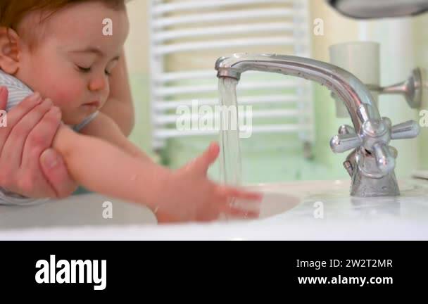 Mom washes her baby's hands in the bathroom. parent is teaching her son ...