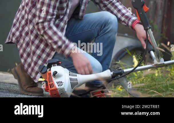 Young Caucasian farmer uses gasoline powered electric scythe to trim ...