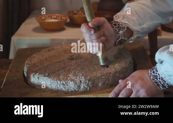 The ancient Quern stone hand mill with grain. The man grinds the grain ...