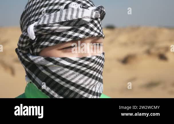 Smart boy in shemagh standing and looking aside in a hot desert in ...
