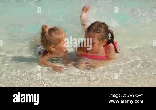 Two sibling girls lay on stomach and splash water in the pool with ...