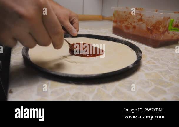 Male arm of cook spreading tomato sauce on pizza dough using a spoon at ...