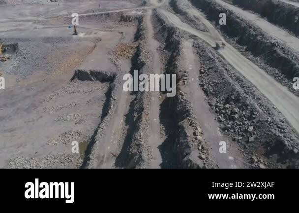 Mining dump trucks in large granite open pit mine. Empty truck rides on road quarry ledge drone ...