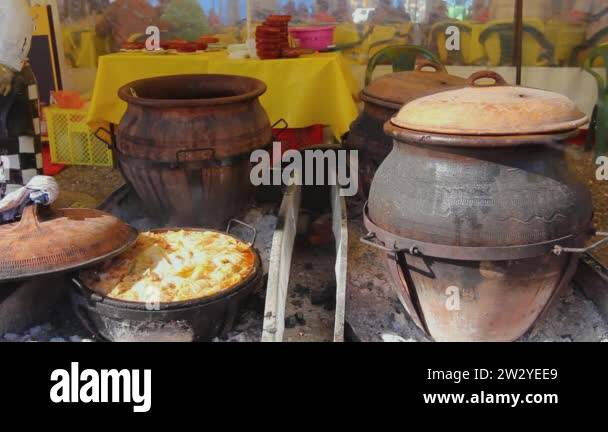 Big amount of food is cooking in a large ceramic, clay pots on embers ...