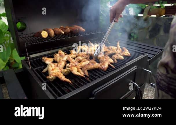4K, Man using metal tongs to turning some spicy chicken wings which are ...