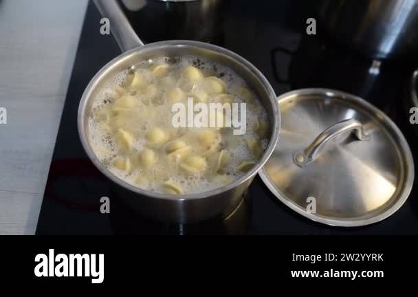Ravioli in pan, boiling water, silver metal background. Cooking Pelmeni, russian dumplings ...