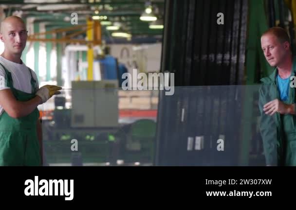 Two Workers in Green Uniform Are Standing, Holding the Sheet of Glass ...