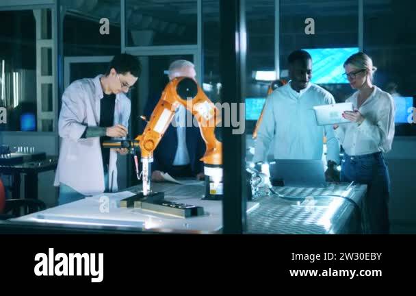Team of industrial robotics engineers working with robot arm. Engineers watching robot ...