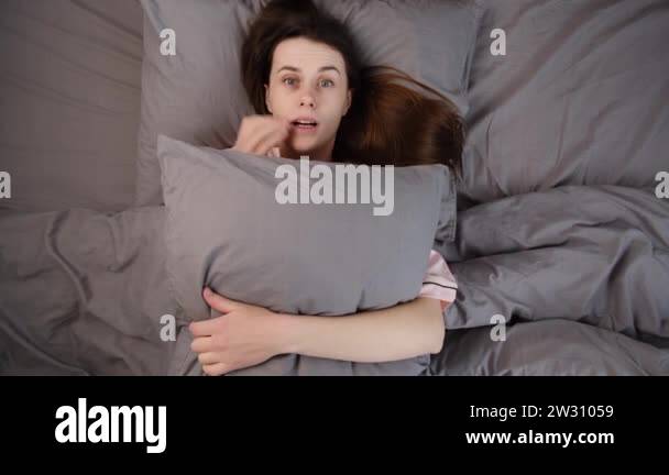 Top view of scared young woman lying in grey bed look at camera feel ...
