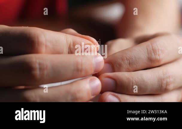 Threading the eye of a needle. Pulling the thread into the needle eye ...