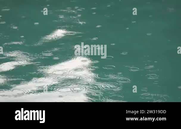 Tropical summer rain splashing into swimming pool. Close up of swimming ...