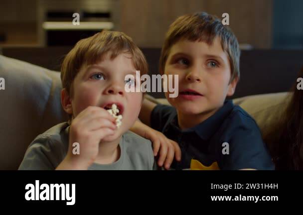 Two brothers watching TV, eating popcorn sitting on couch at home. Two ...