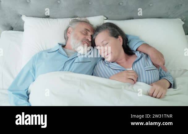Elderly husband and wife sleeping together in bed, couple hugging at ...