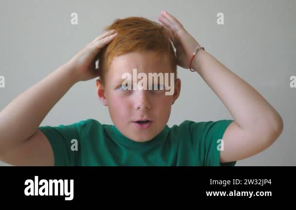 Close up of adorable red-haired boy grabbing his head and showing joy ...