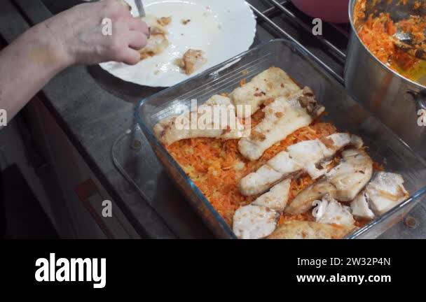 Arranging fried pieces of fish on cooked chopped vegetables to form one ...