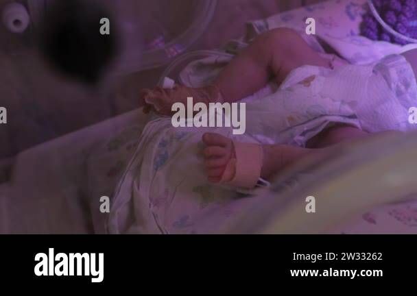 Close up side view of baby feet in incubator, with sensors and tubes ...