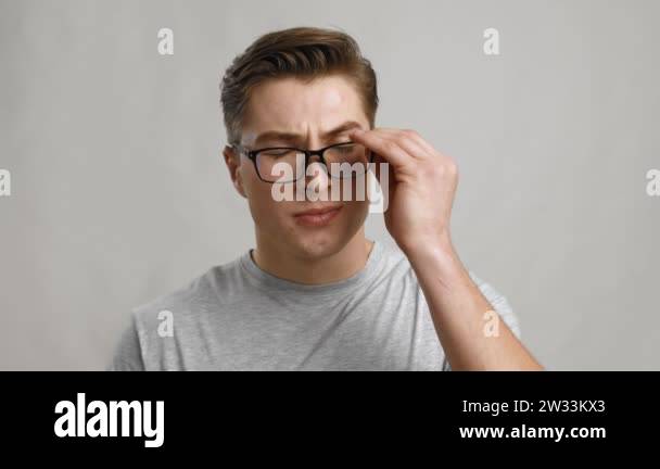 Young tired man taking off his glasses and rubbing his eyes, grey ...