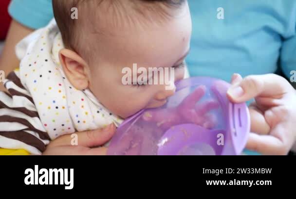 mother holds the baby in her arms and feeds her boy with a spoon ...