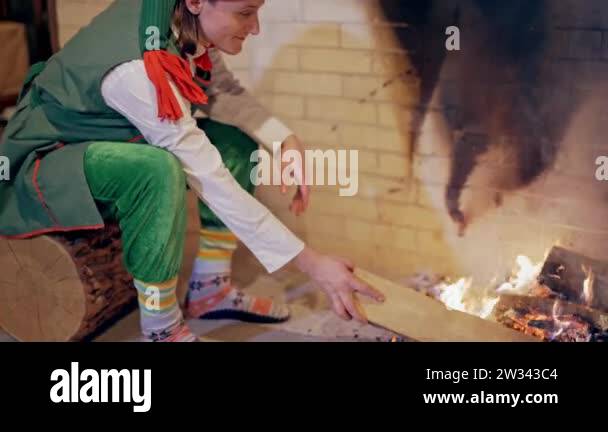 Man in a festive costume of elf is putting logs into the open fire in ...