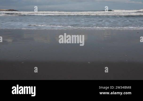 Ocean tide water waves roll up on to the beach shore as scene shows ...