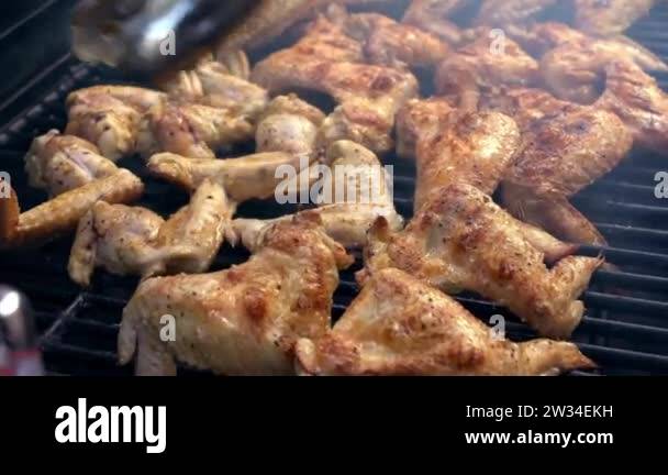 Man using metal tongs to turning some spicy chicken wings which are ...