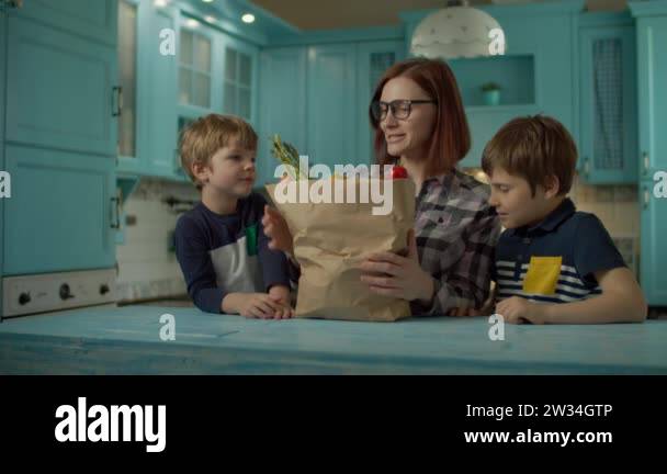 Two kids help young 30s mother to unpack paper bag with fresh food ...