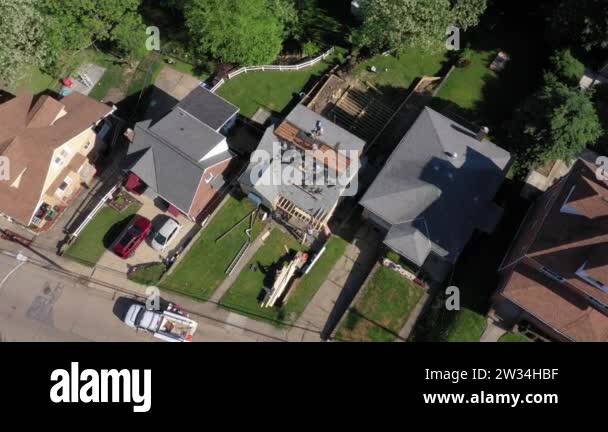 A high orbiting aerial flyover of roofers removing the shingles of a ...